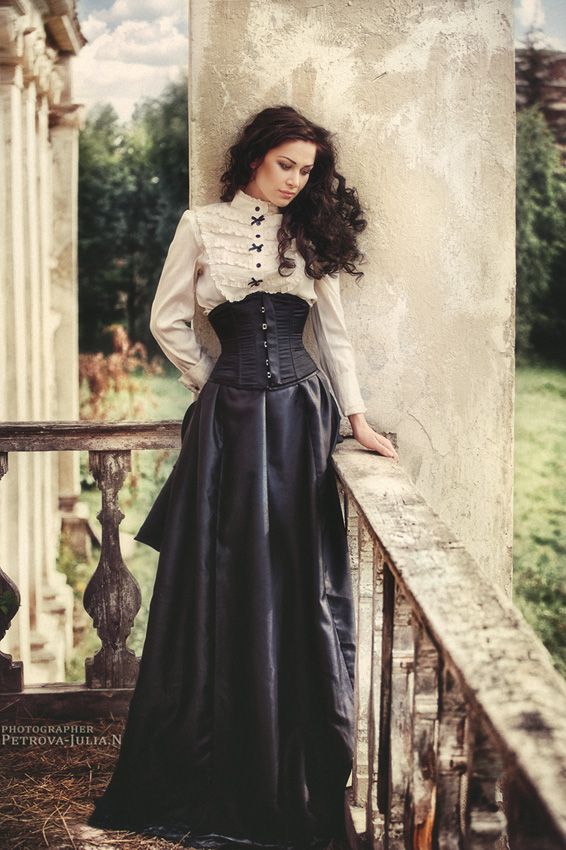 Vesta in long black skirt, white blouse, and under-bust corset | Scrolller