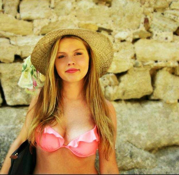 Attractive girl in a bikini, standing by a wall. She is also wearing a hat. | Scrolller