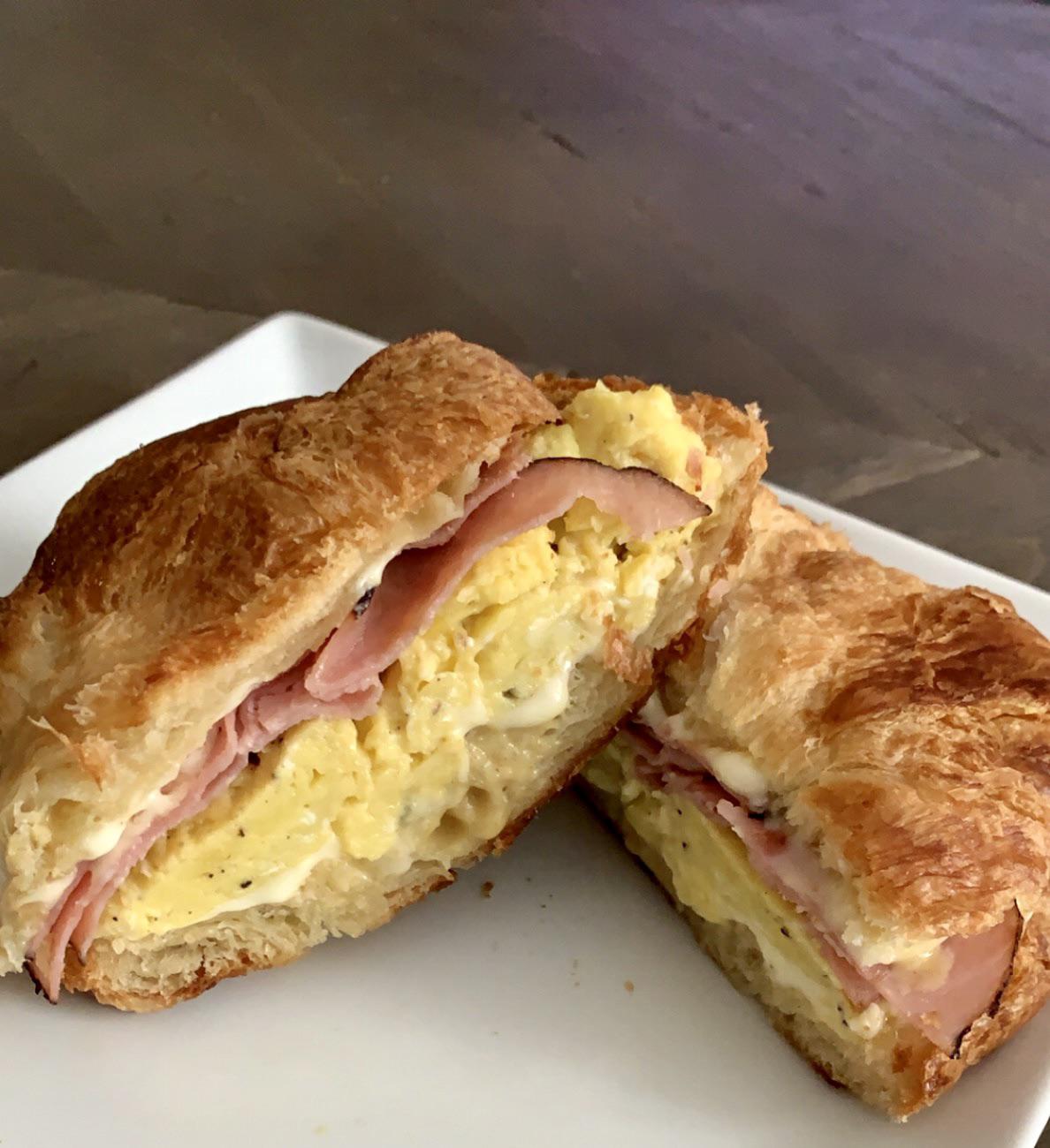 Black Forest ham, Swiss cheese, and fluffy scrambled eggs on a buttery croissant, with a honey ...