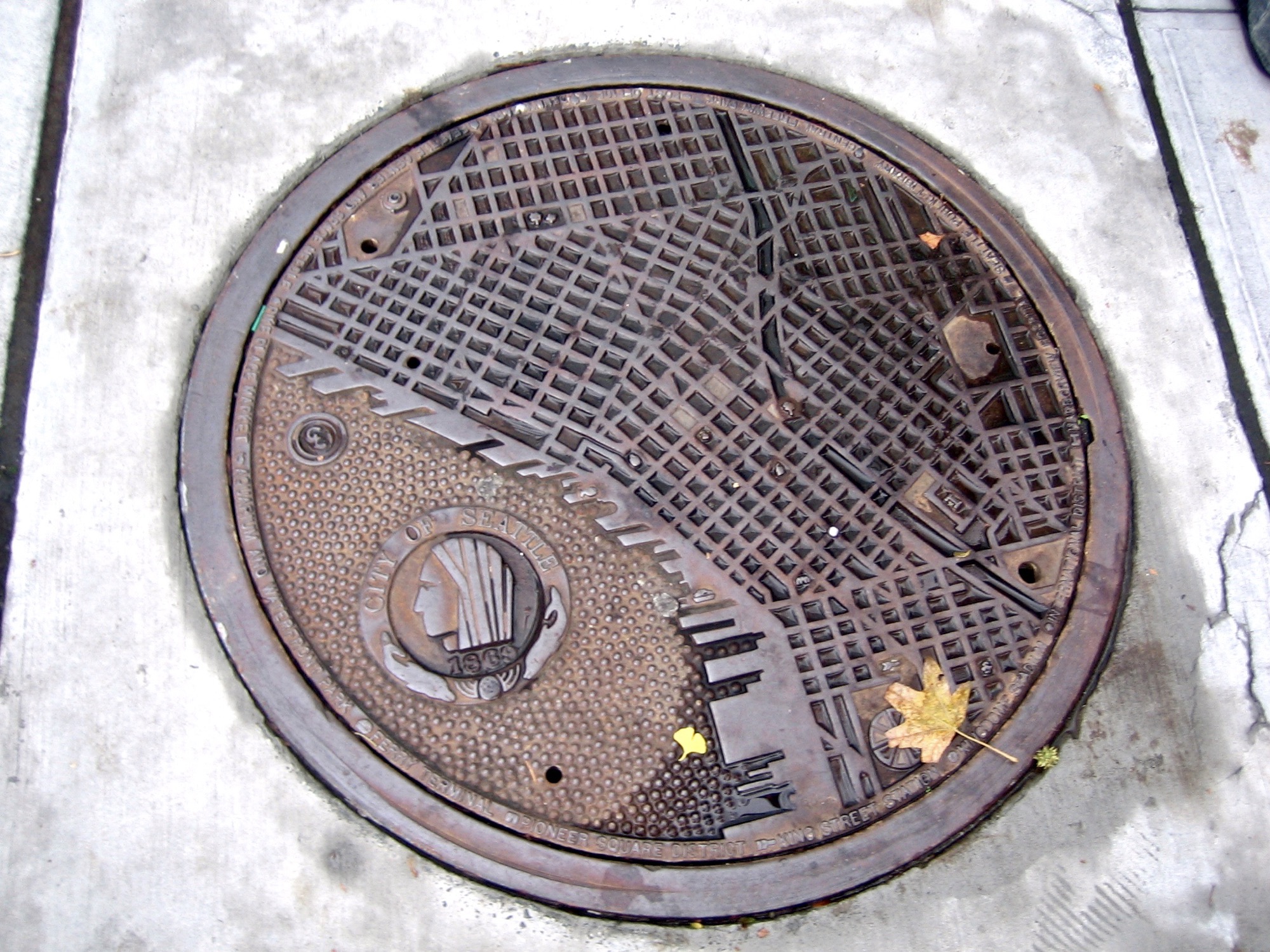 Seattle manhole covers have a city map on them with markers for important locations. There’s a ...