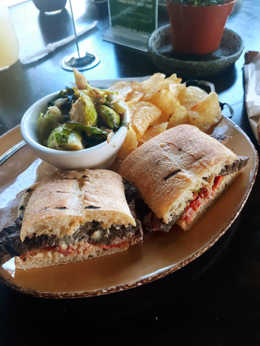 Steak and red pepper sandwich with a side of chips and brussel sprouts. | Scrolller