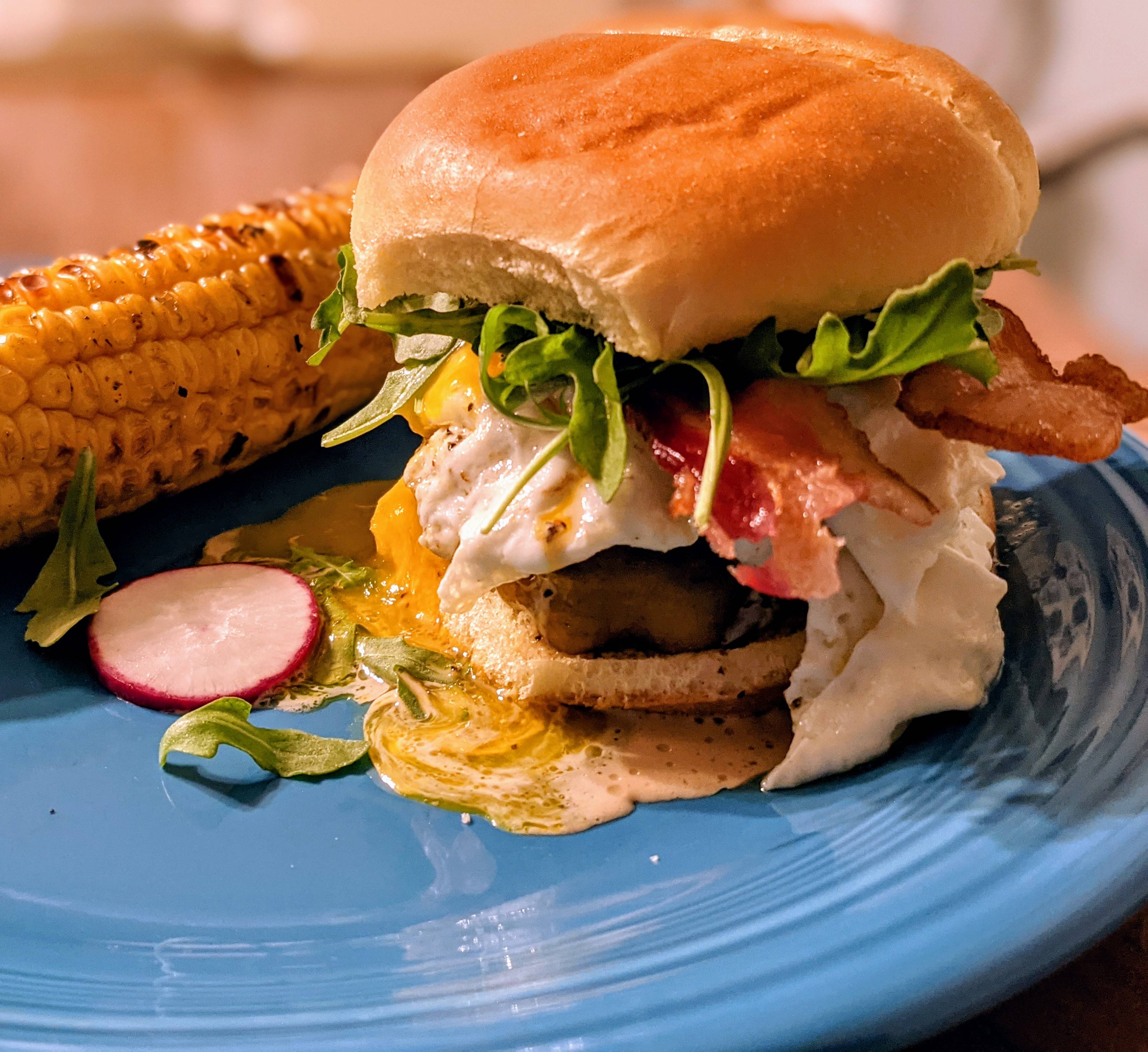 Burger with fried egg, bacon, cheddar cheese, radish, and arugula/grilled corn on the cob ...