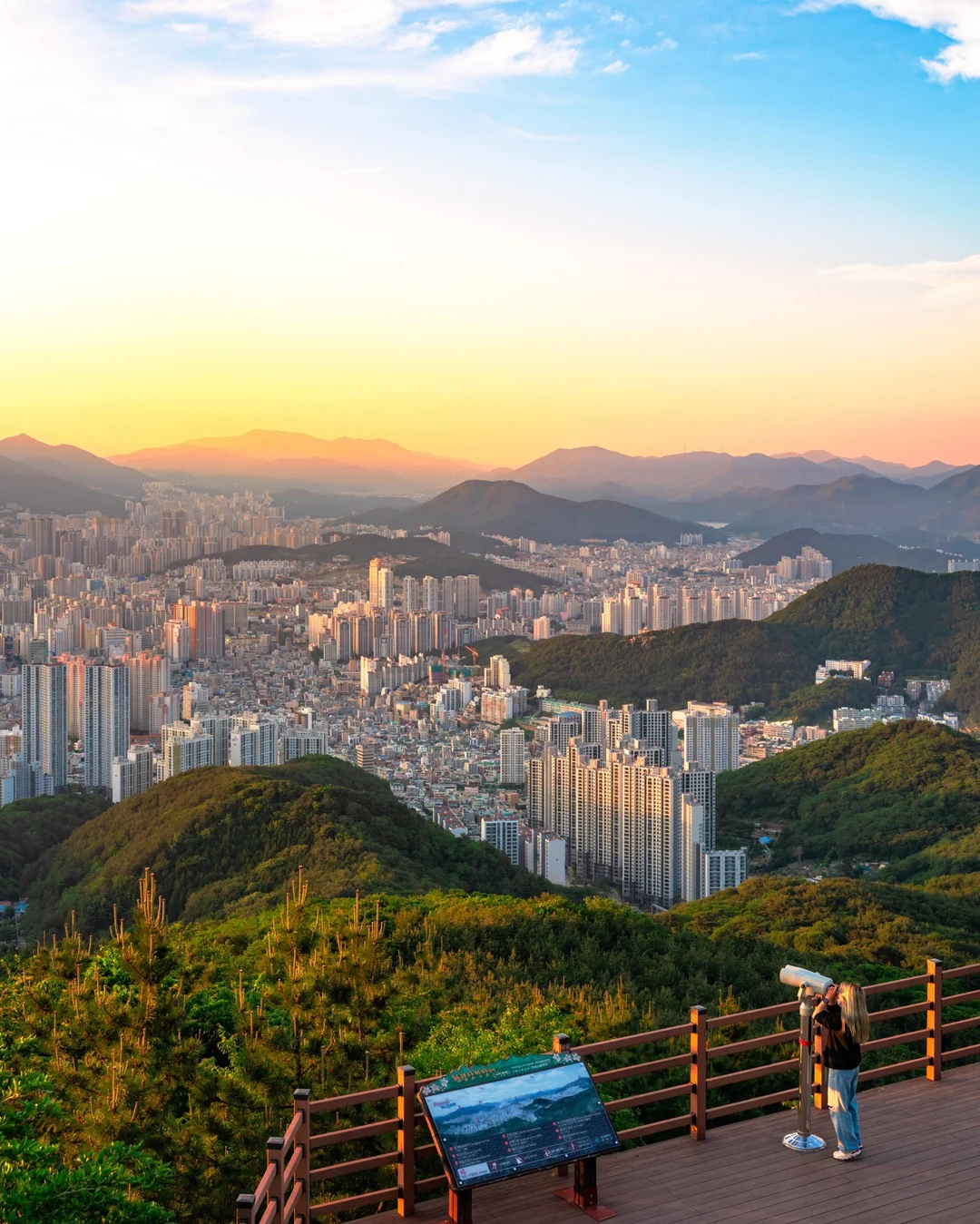 Mt Hwangnyeong observatory deck overlooking the mountainous cityscape of Busan during sunset ...