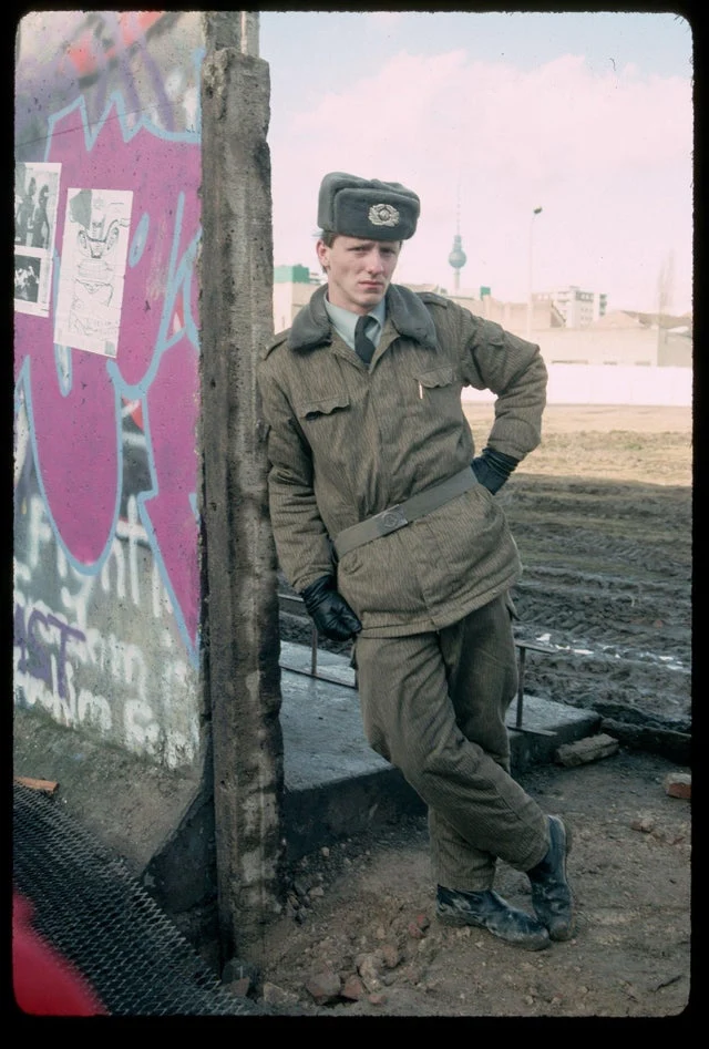 East German soldier leans against a remnant of the Berlin Wall (early 1990) | Scrolller